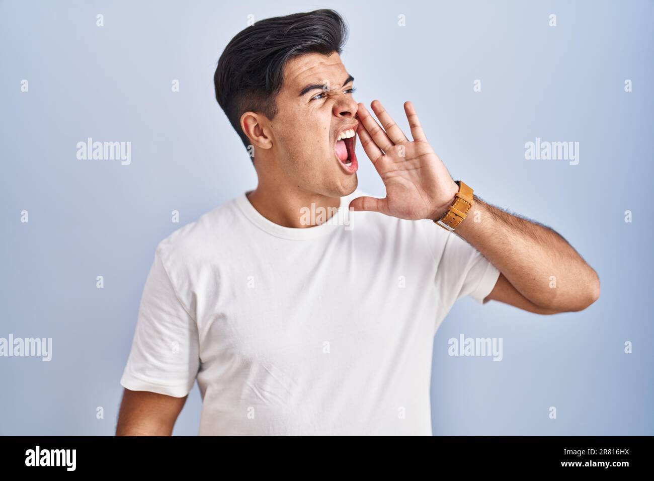 Hispanic man standing over blue background shouting and screaming loud ...