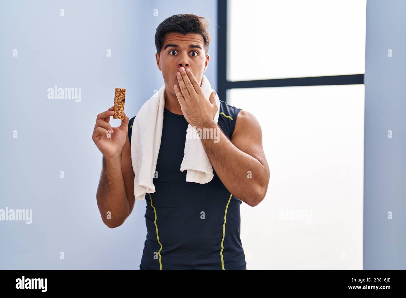 Hispanic man eating protein bar as healthy energy snack covering mouth ...