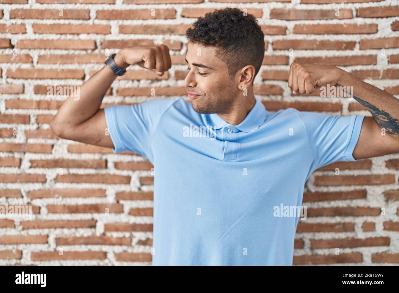 Brazilian young man standing over brick wall showing arms muscles ...
