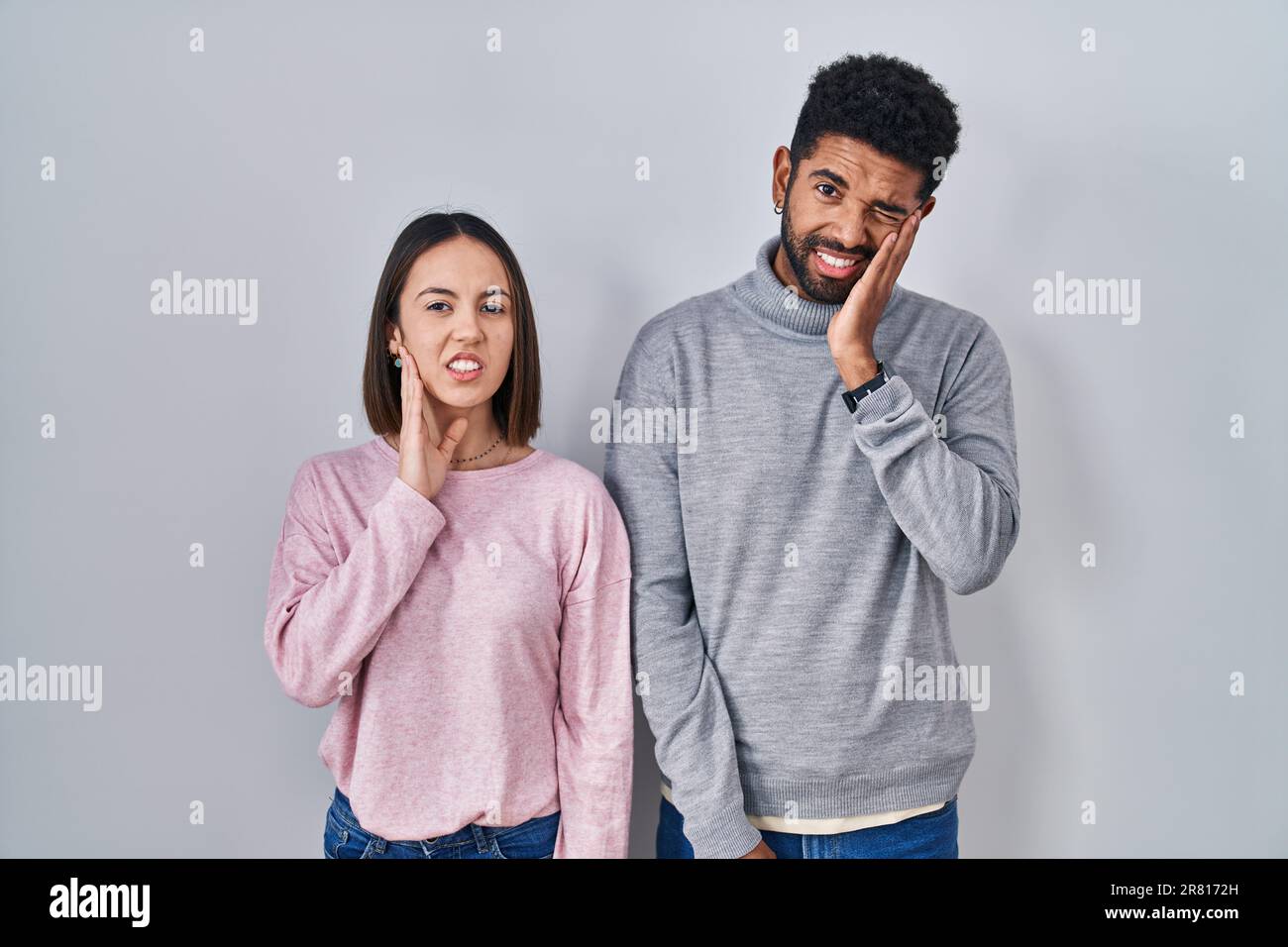 Young hispanic couple standing together touching mouth with hand with ...