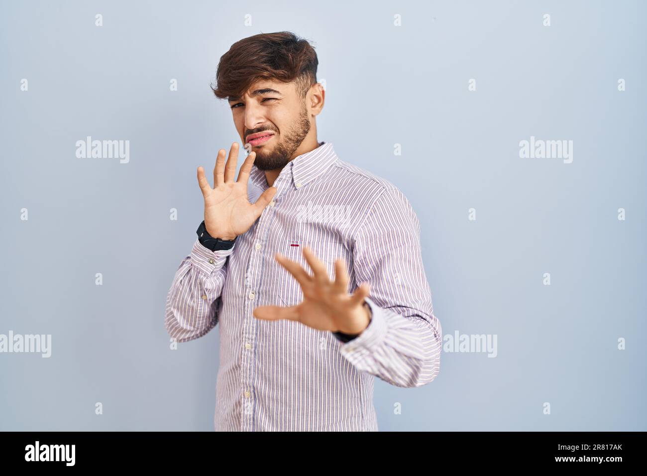 Arab man with beard standing over blue background disgusted expression ...