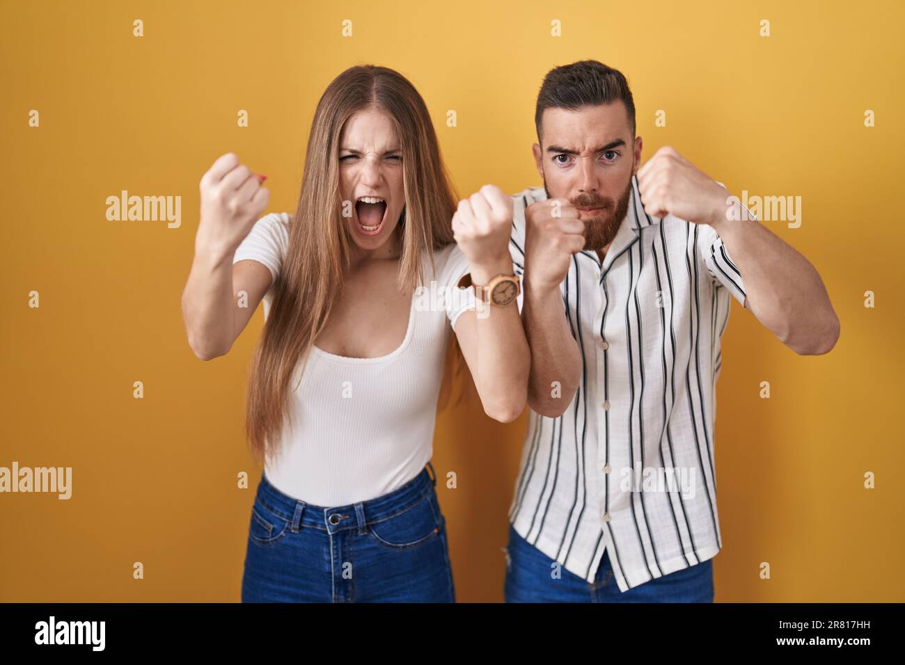 Young couple standing over yellow background angry and mad raising ...