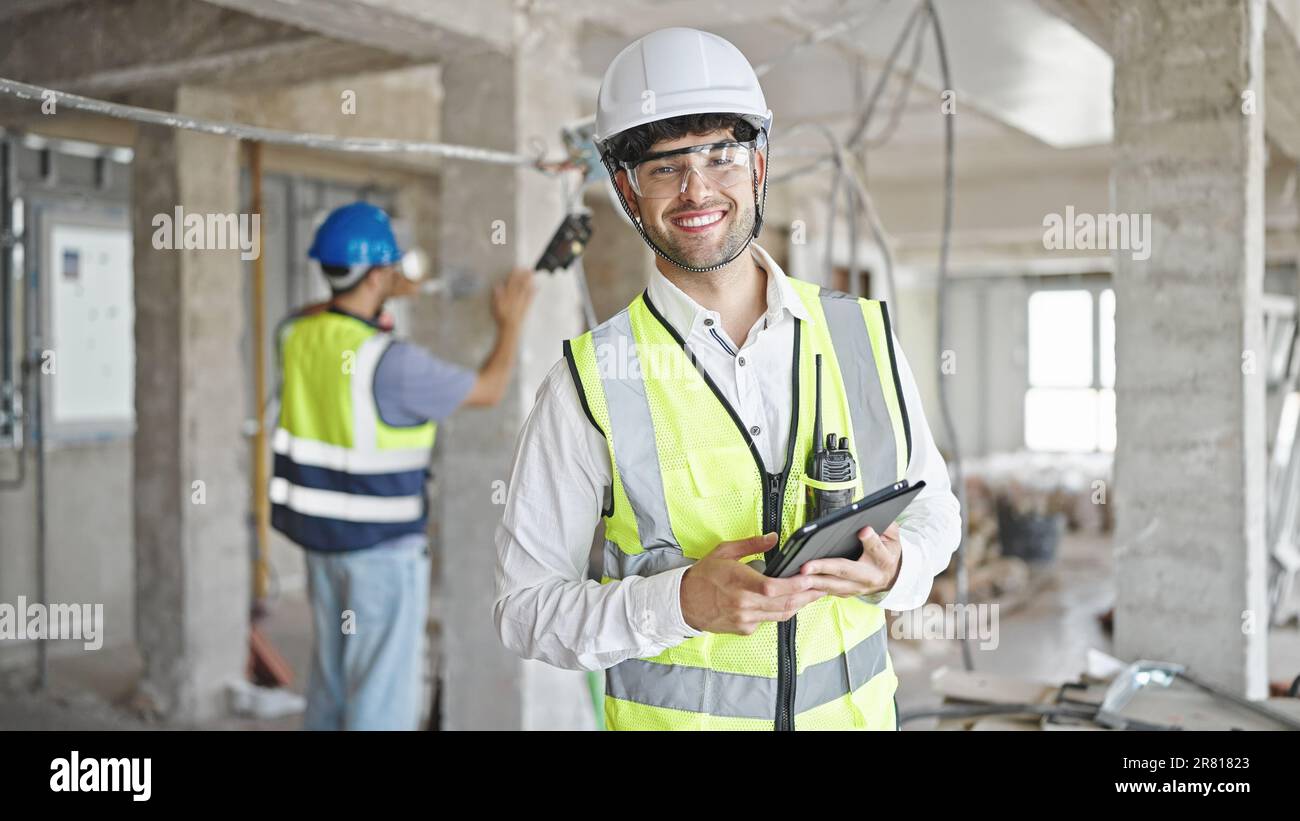 Two men builders smiling confident using touchpad at construction site ...