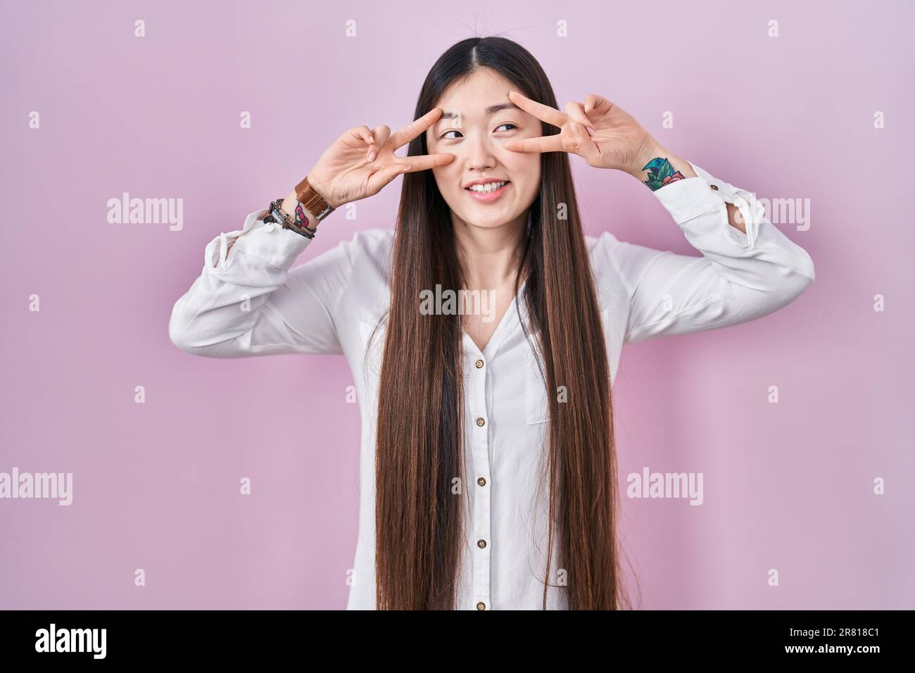Chinese young woman standing over pink background doing peace symbol ...