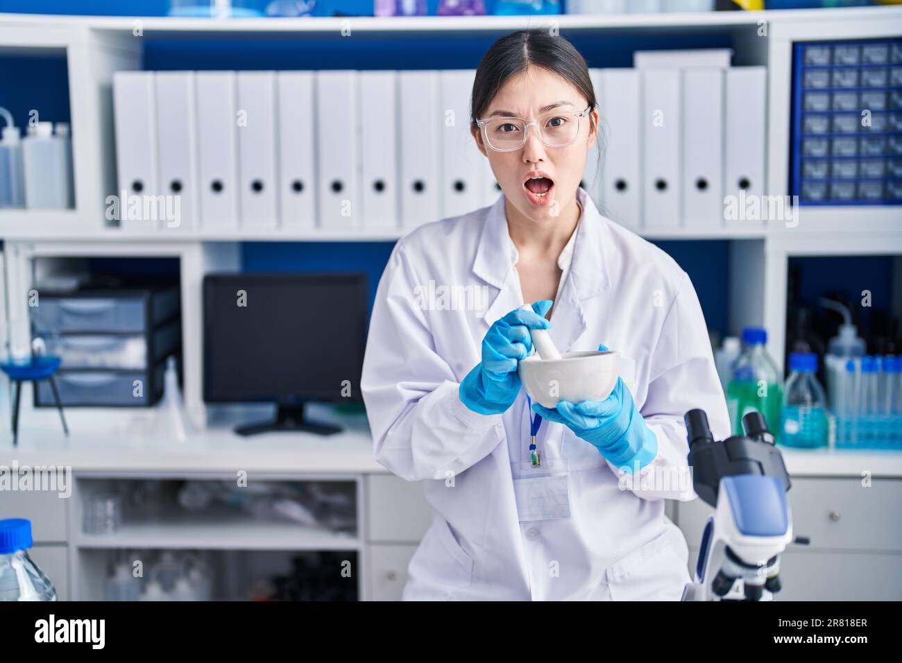 Chinese young woman working at scientist laboratory mixing in shock ...