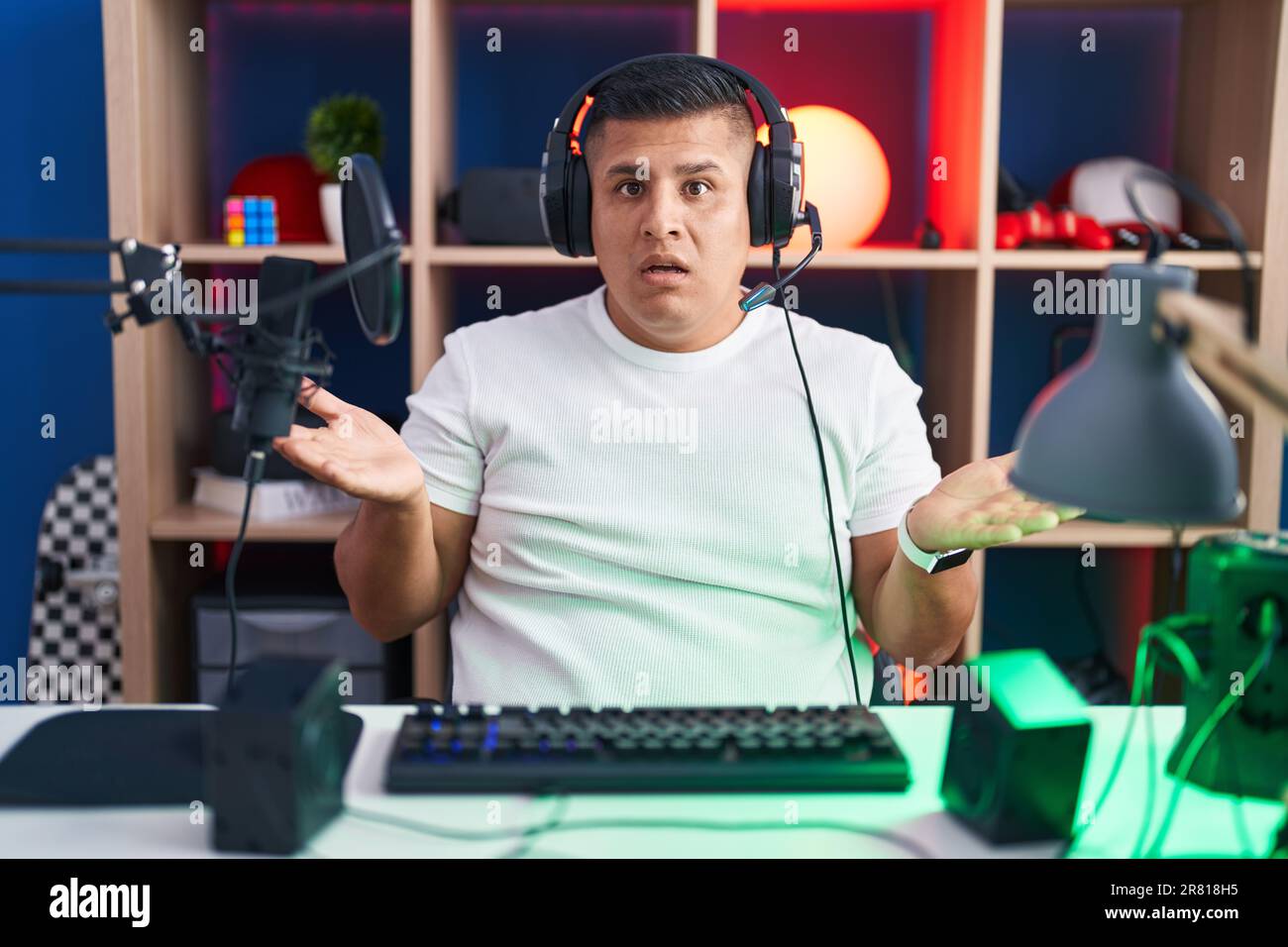 Young hispanic man playing video games clueless and confused with open ...