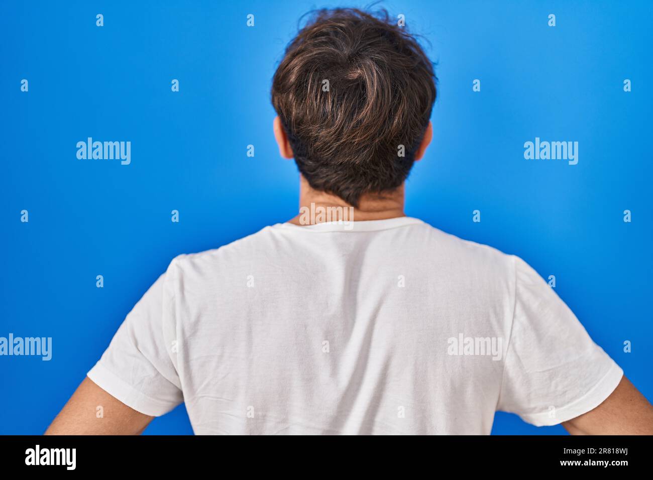 Hispanic young man standing over blue background standing backwards ...