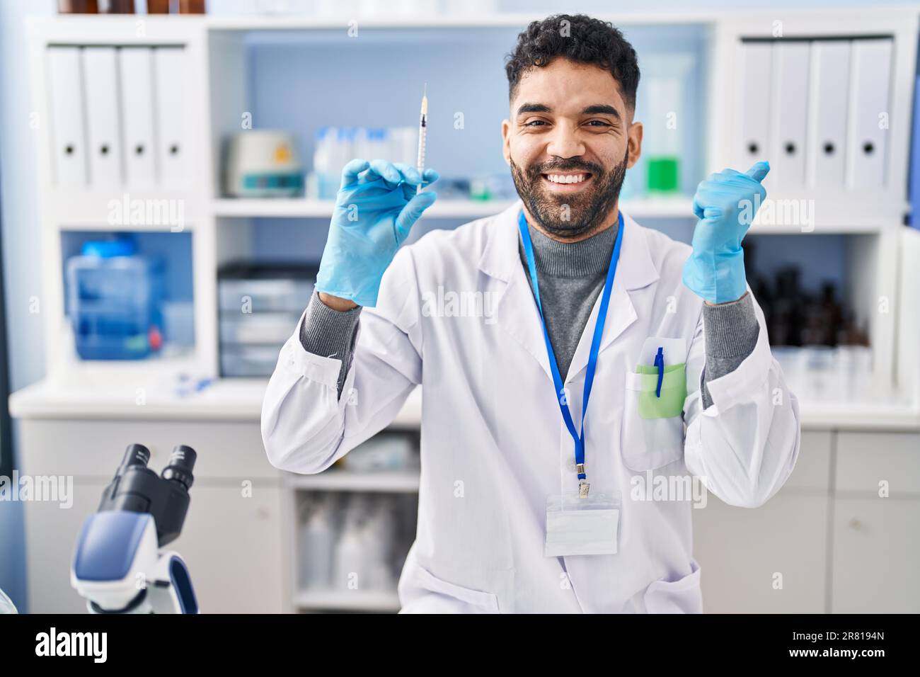 Hispanic man with beard working at scientist laboratory holding syringe ...