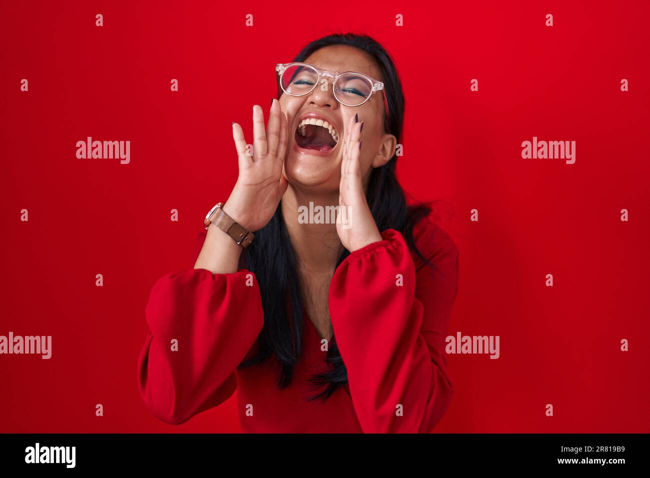 Asian young woman standing over red background shouting angry out loud ...