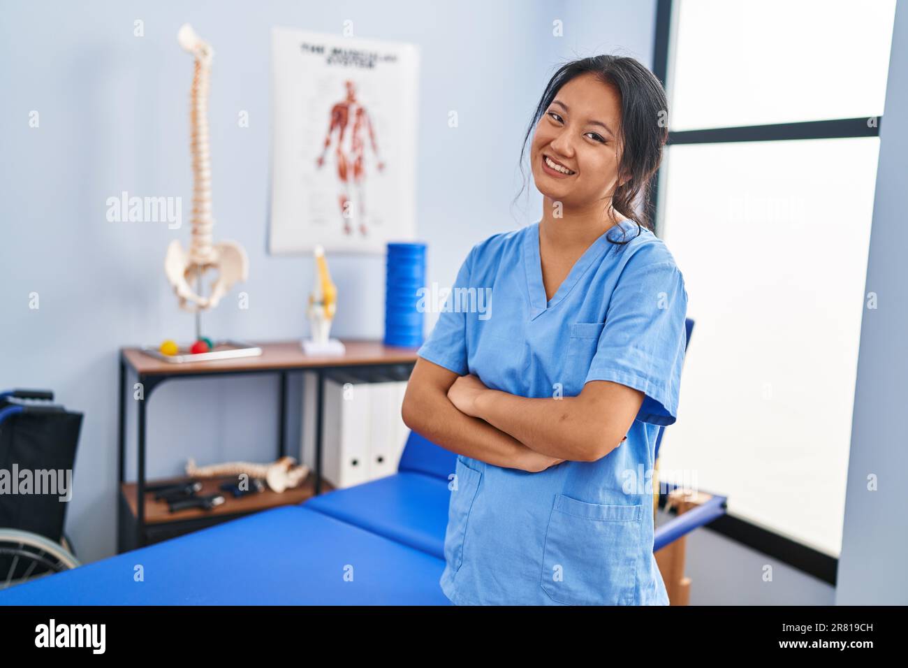 Young chinese woman wearing physiotherapist uniform standing with arms ...