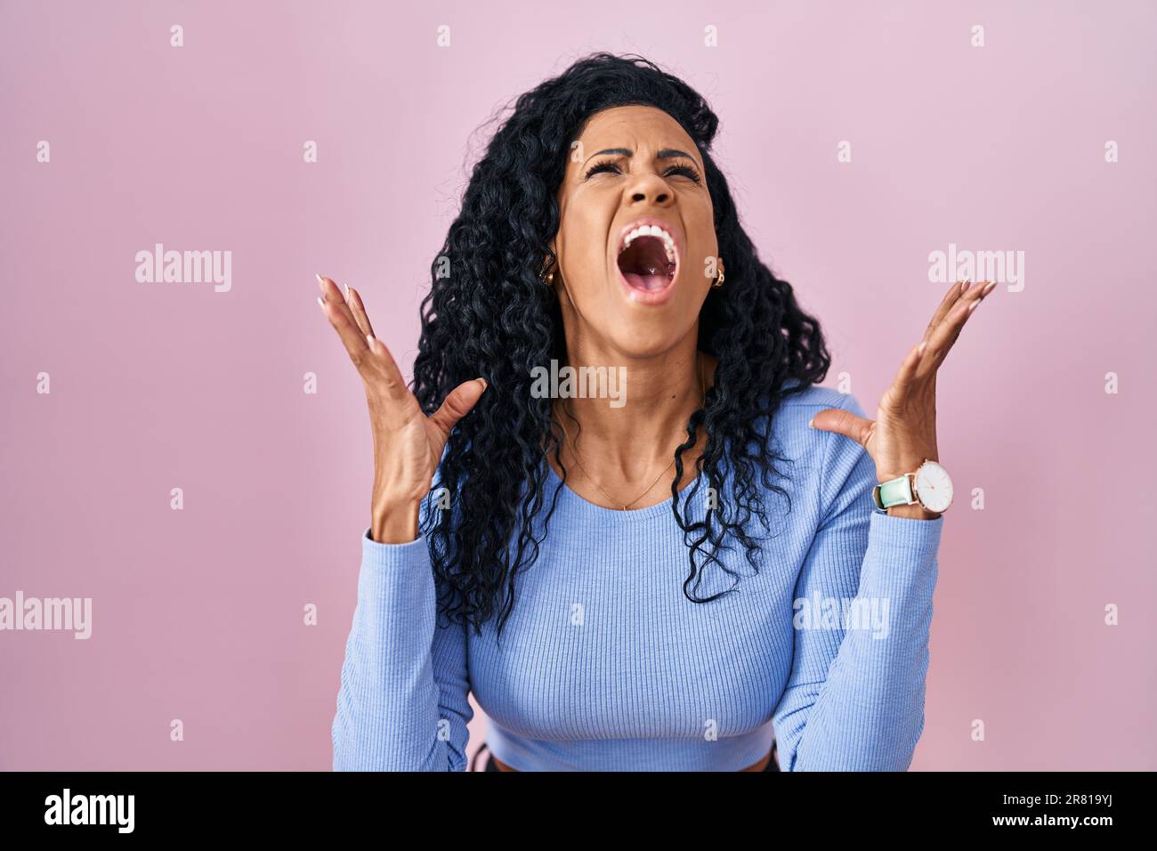 Middle age hispanic woman standing over pink background crazy and mad ...
