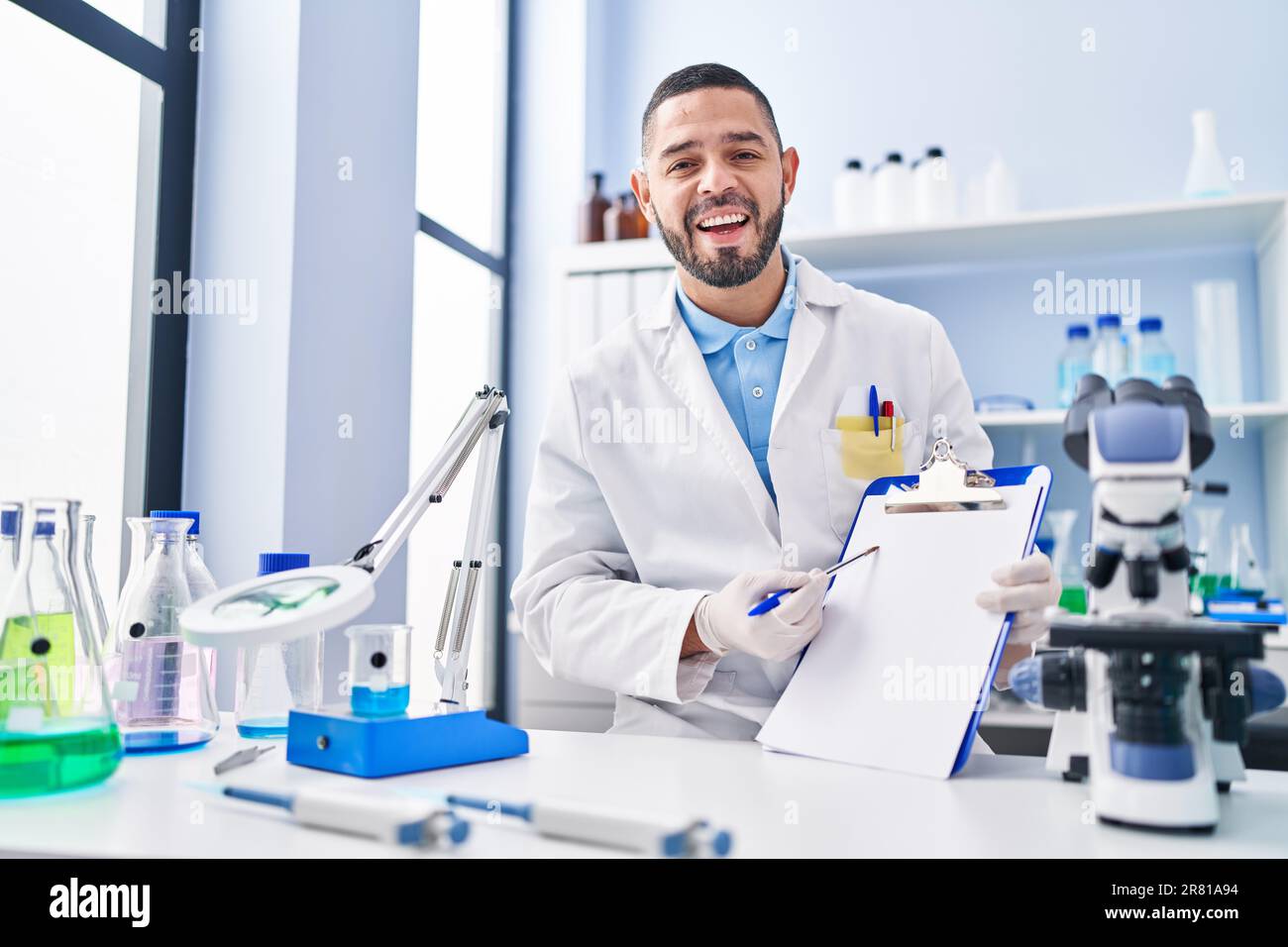 Hispanic man working at scientist laboratory holding blank clipboard ...