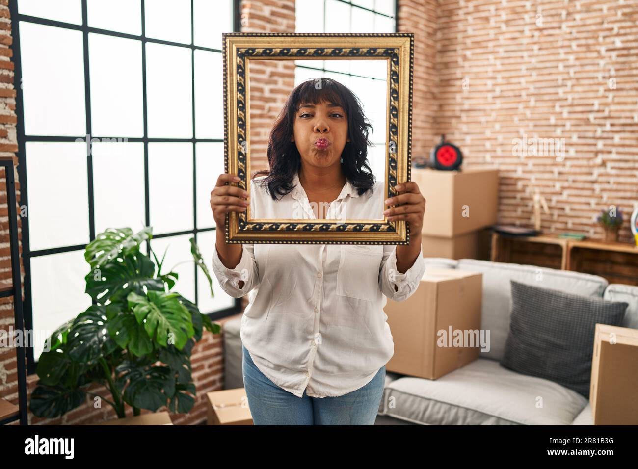 Hispanic woman at new home holding empty frame puffing cheeks with ...