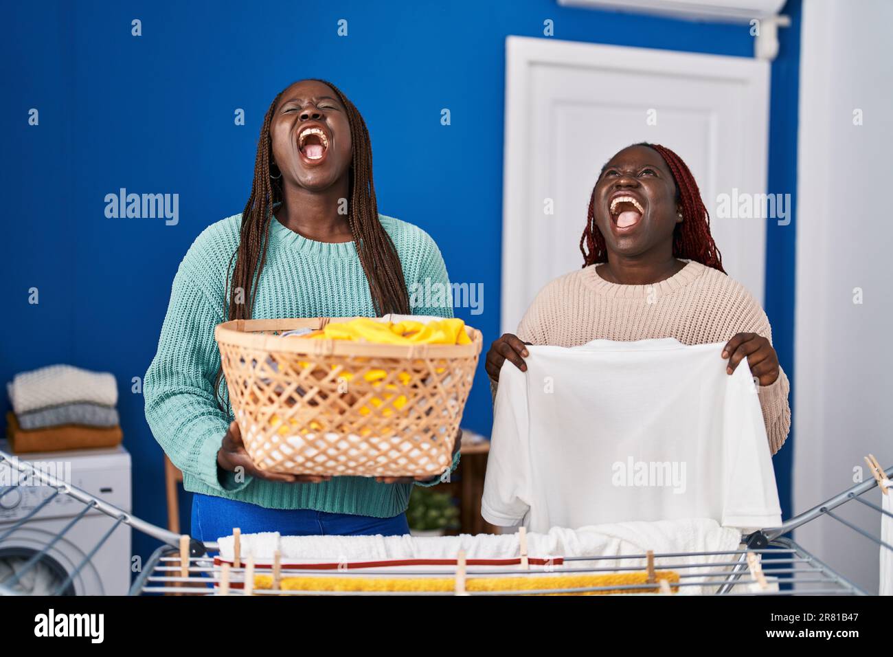 Two african women hanging clothes at clothesline angry and mad ...