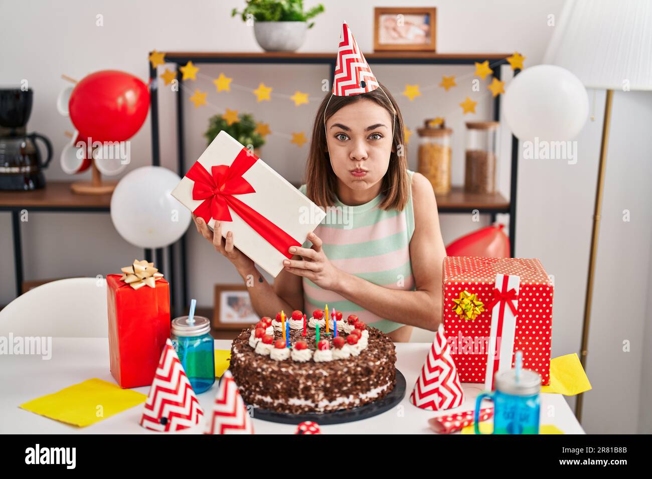 Hispanic woman celebrating birthday with cake holding gift puffing ...