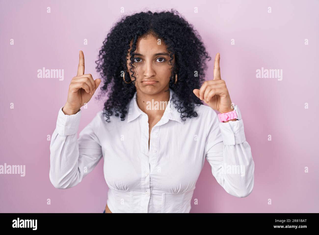 Hispanic woman with curly hair standing over pink background pointing ...