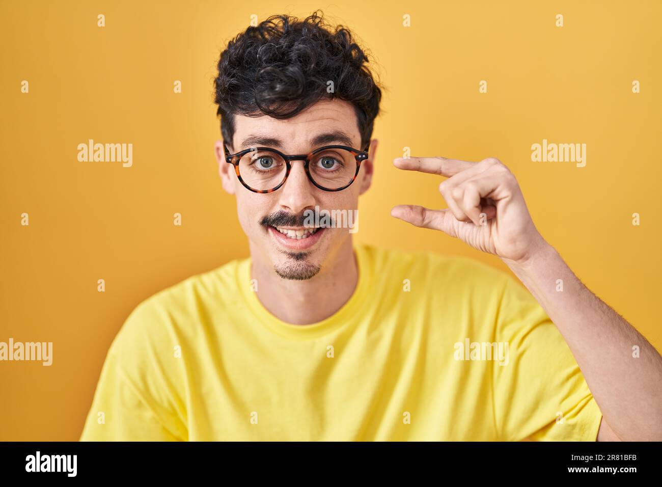 Hispanic man wearing glasses standing over yellow background smiling ...
