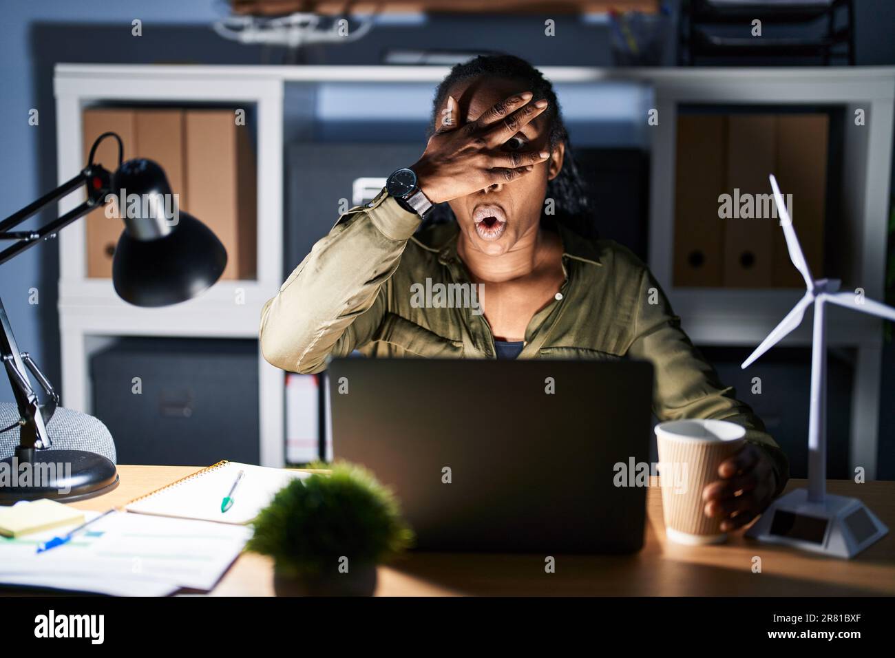 African woman working using computer laptop at night peeking in shock ...