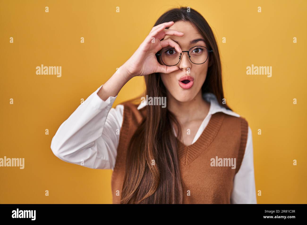 Young brunette woman standing over yellow background wearing glasses ...