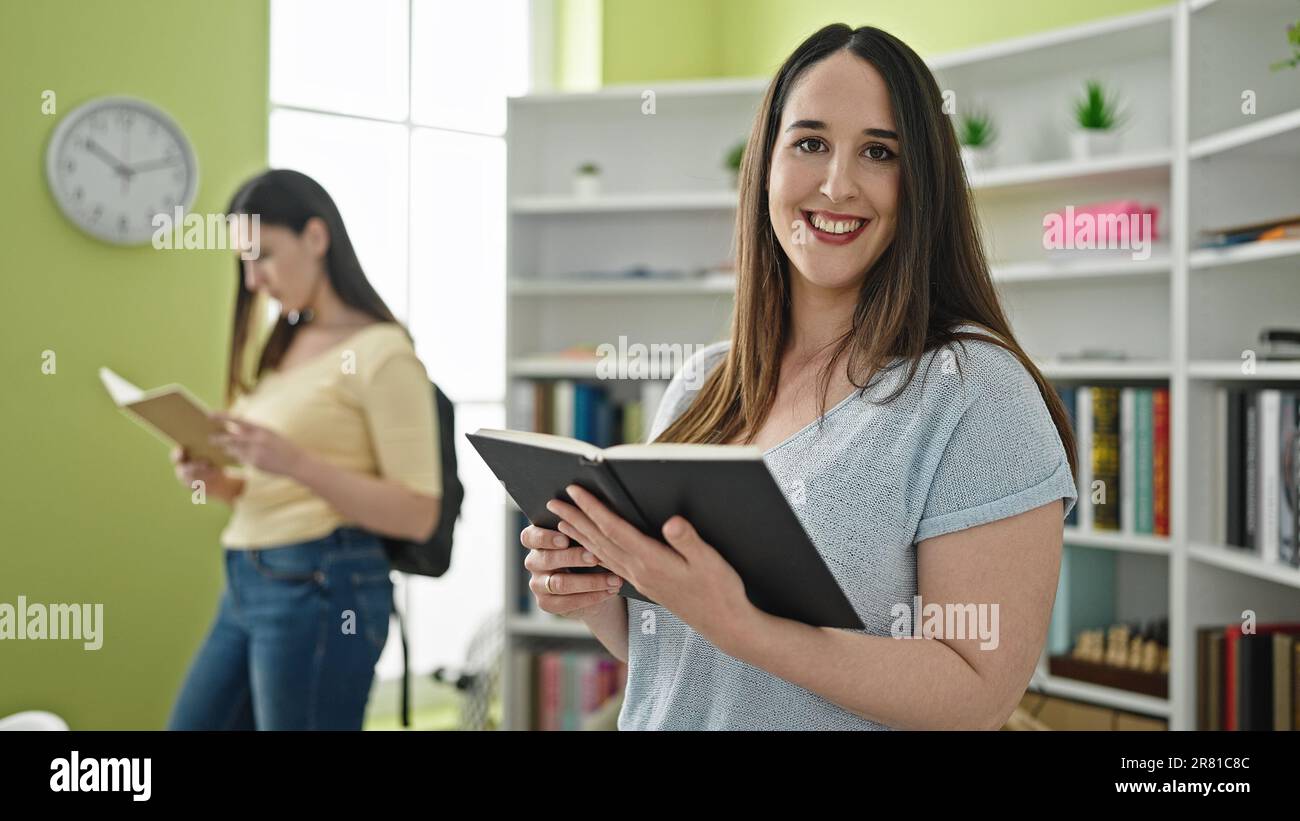 Two women standing reading books at library university Stock Photo - Alamy