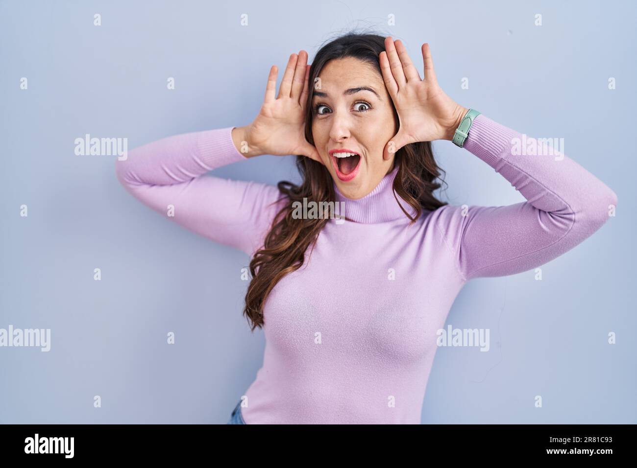 Young brunette woman standing over blue background smiling cheerful ...