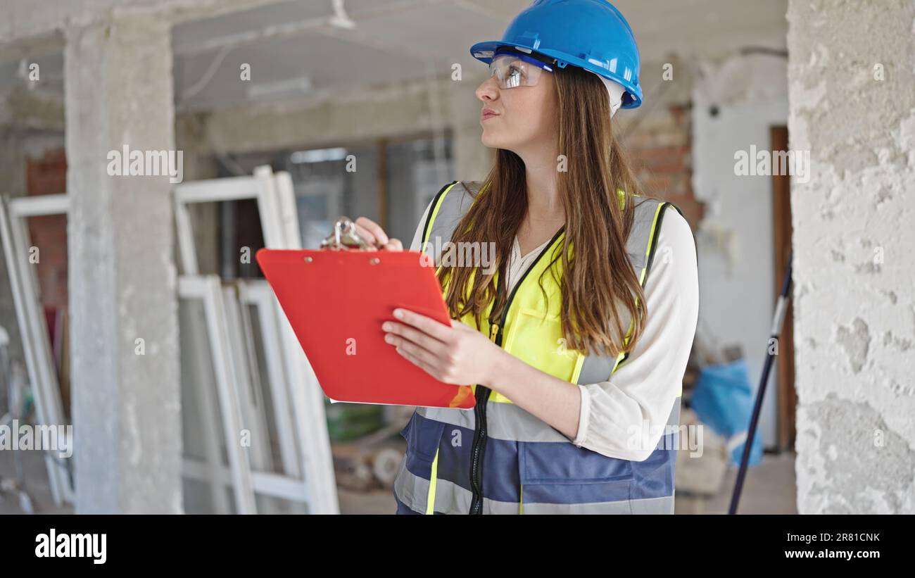 Young beautiful hispanic woman builder writing on clipboard at ...