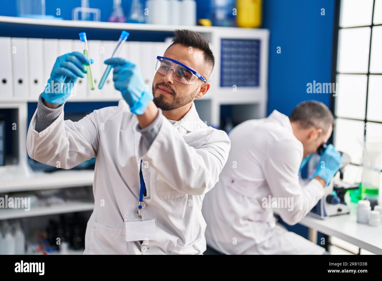 Two men scientists holding test tubes using microscope at laboratory ...