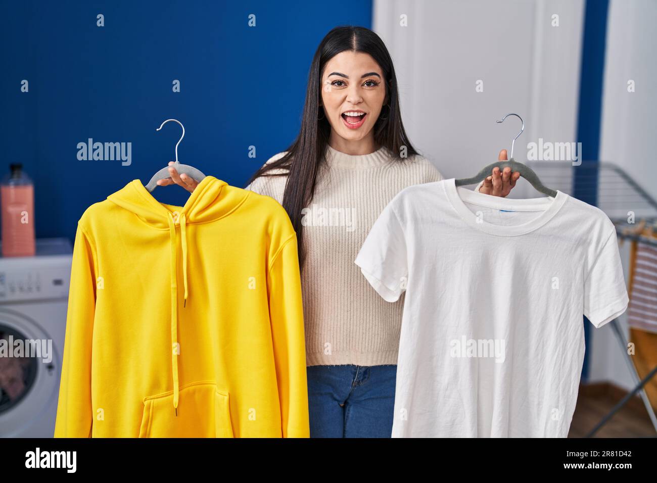 Young woman hanging clothes on racks angry and mad screaming frustrated ...