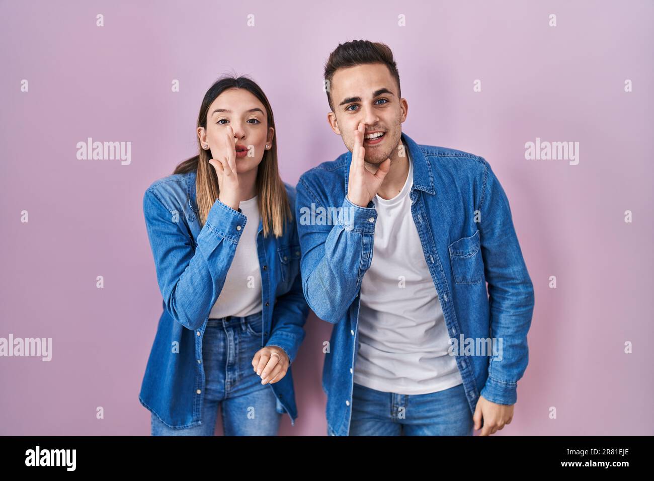 Young hispanic couple standing over pink background hand on mouth ...