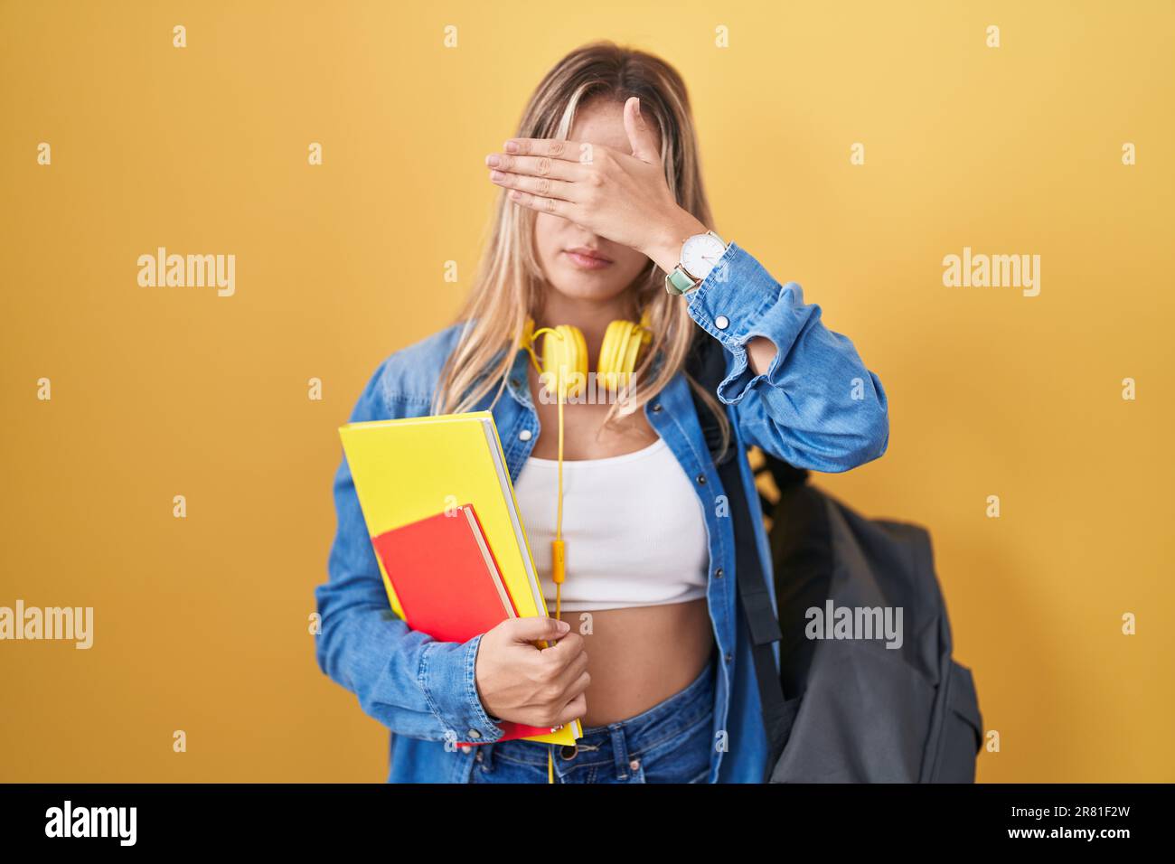 Young blonde woman wearing student backpack and holding books covering ...