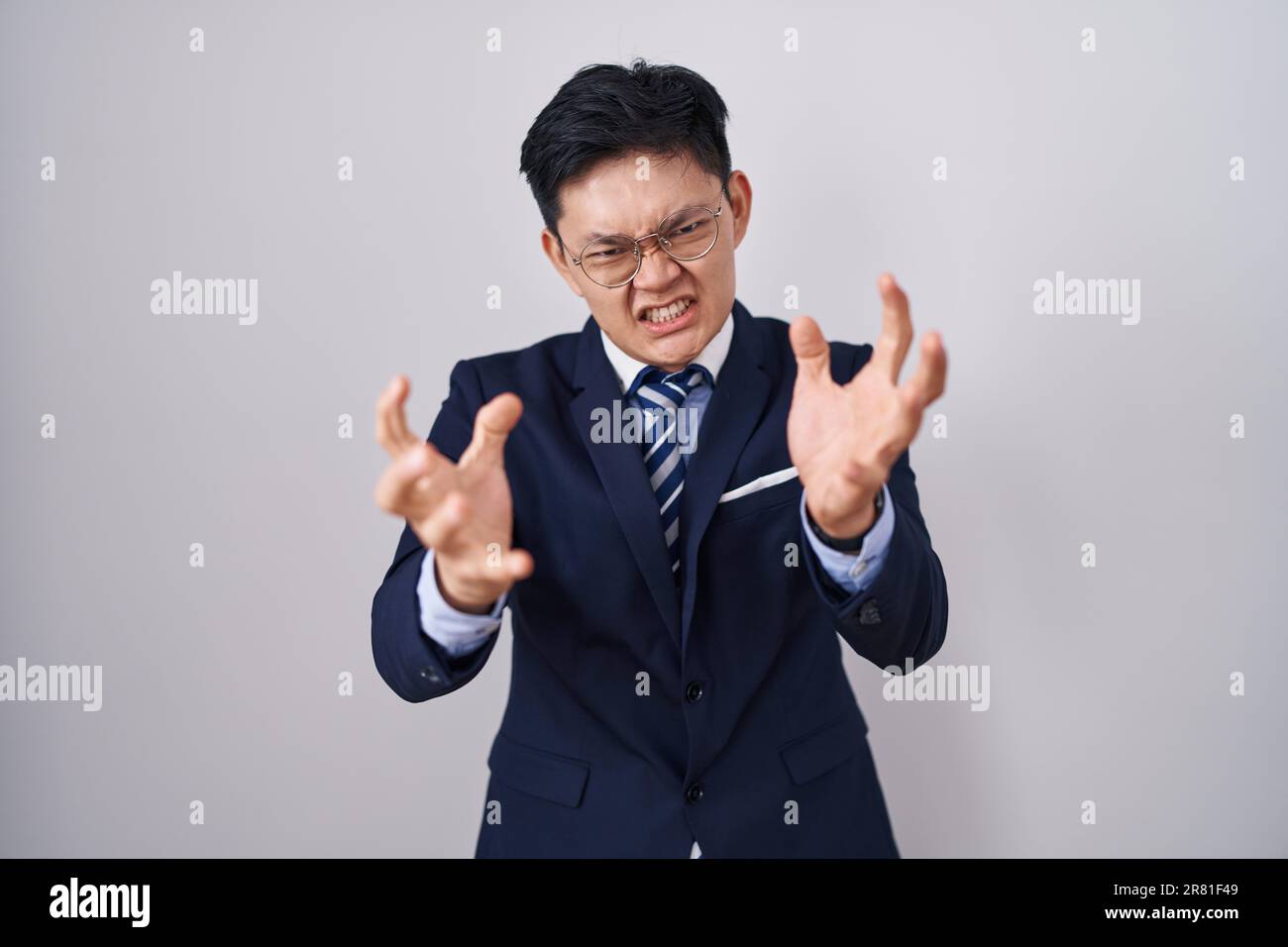 Young asian man wearing business suit and tie shouting frustrated with ...