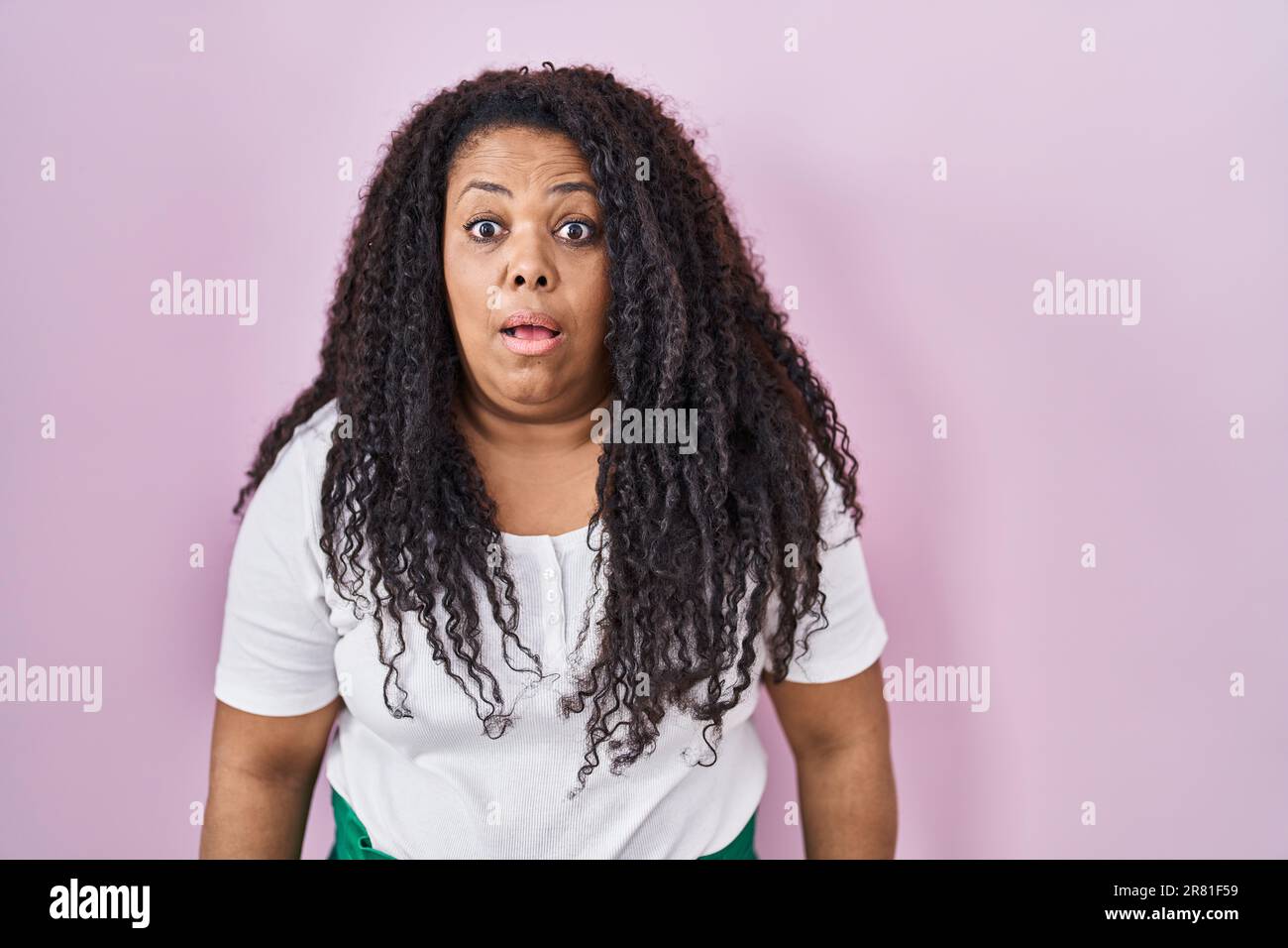 Plus size hispanic woman standing over pink background afraid and ...