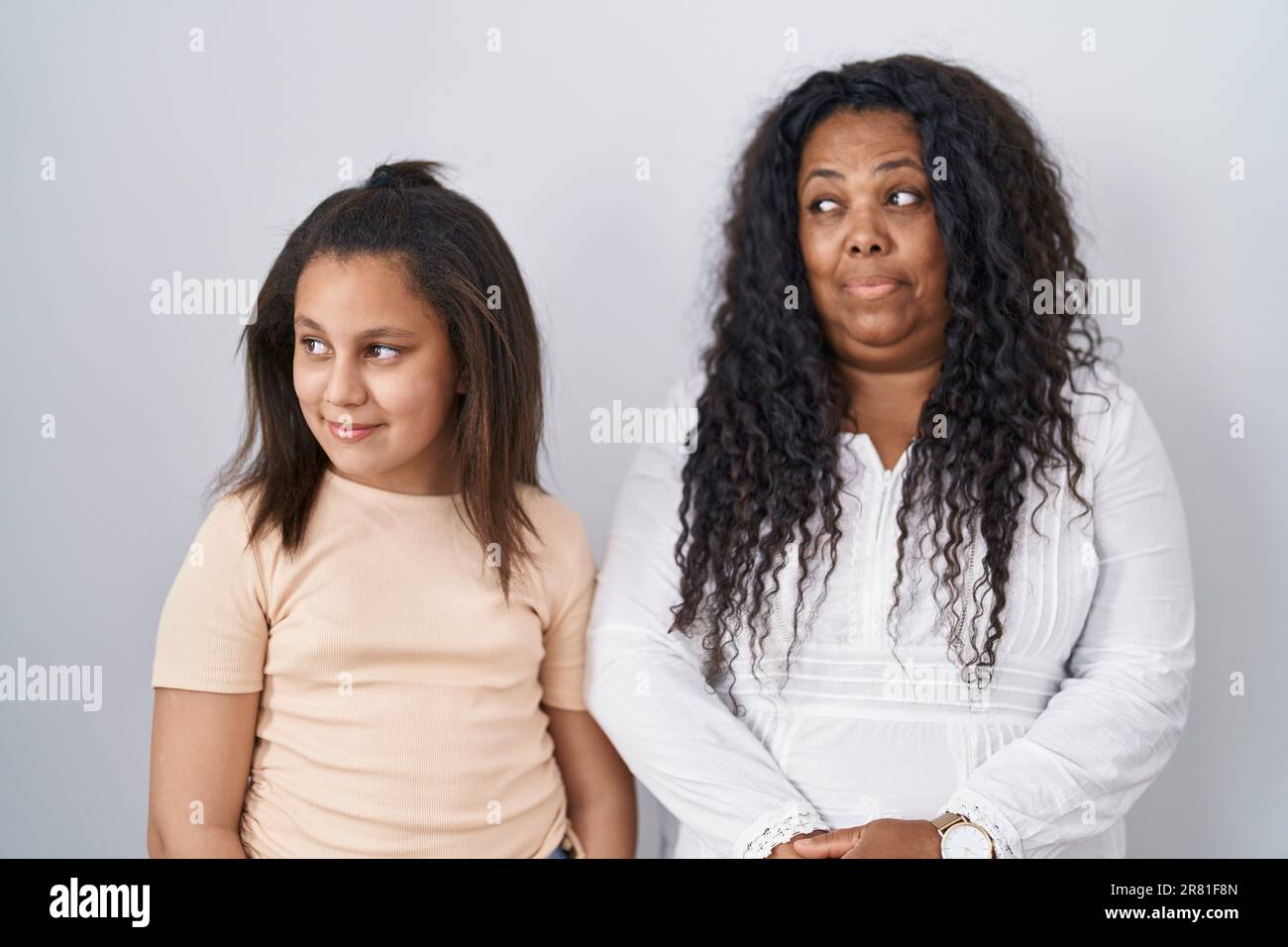 Mother and young daughter standing over white background smiling ...