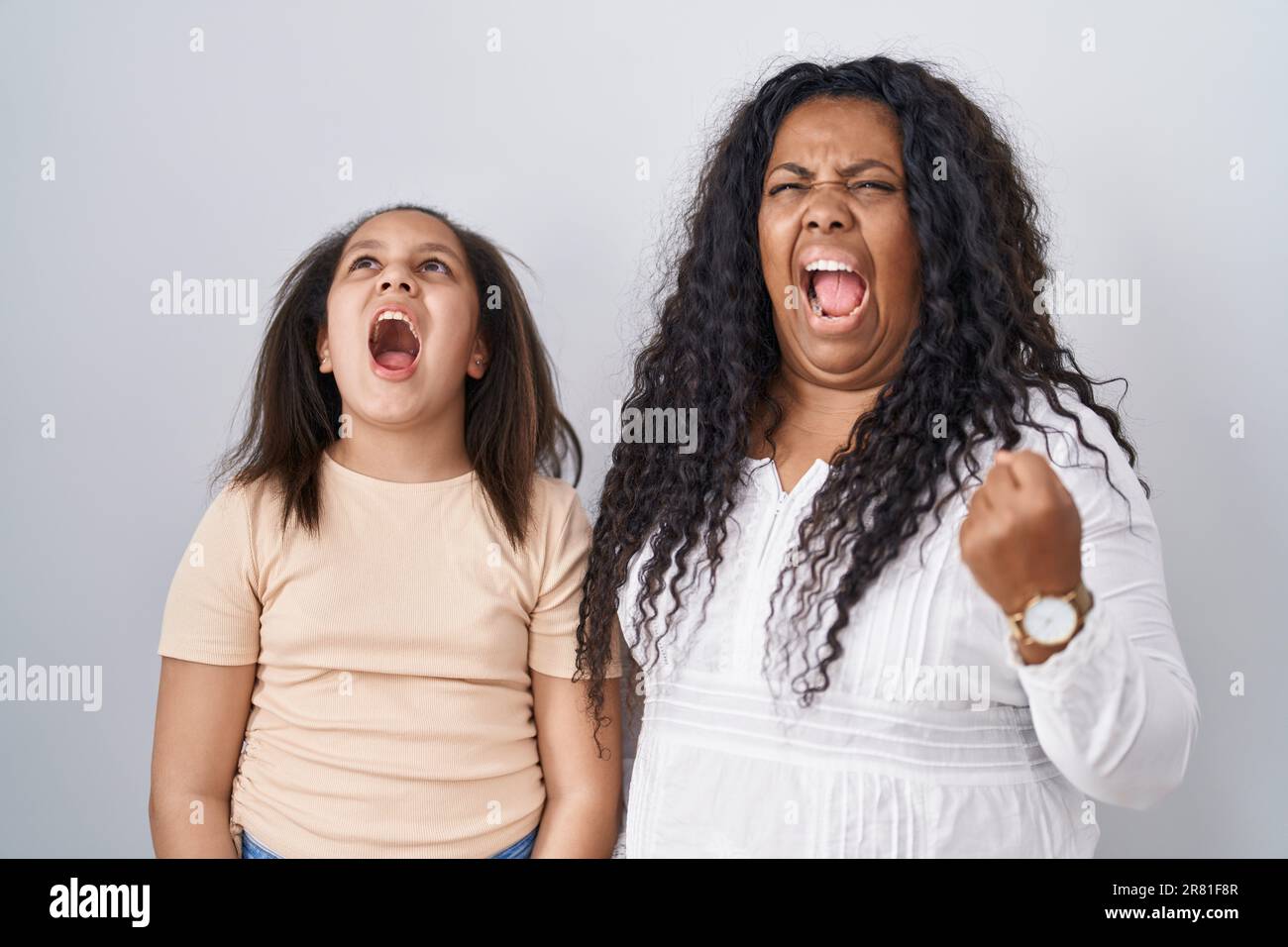 Mother and young daughter standing over white background angry and mad ...