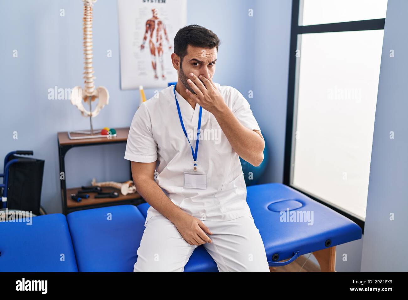 Young hispanic man with beard working at pain recovery clinic smelling ...