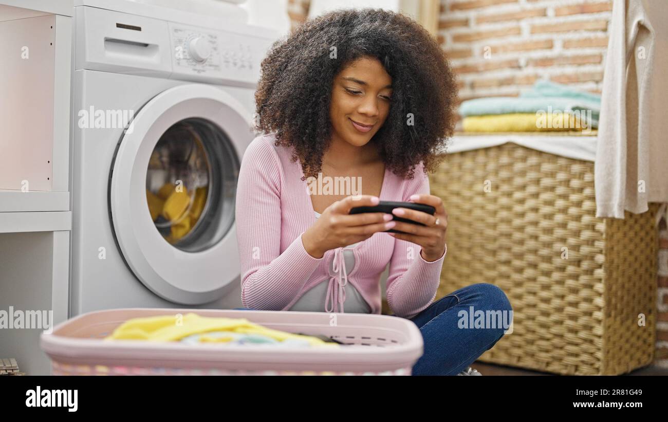 African american woman watching video on smartphone waiting for washing ...