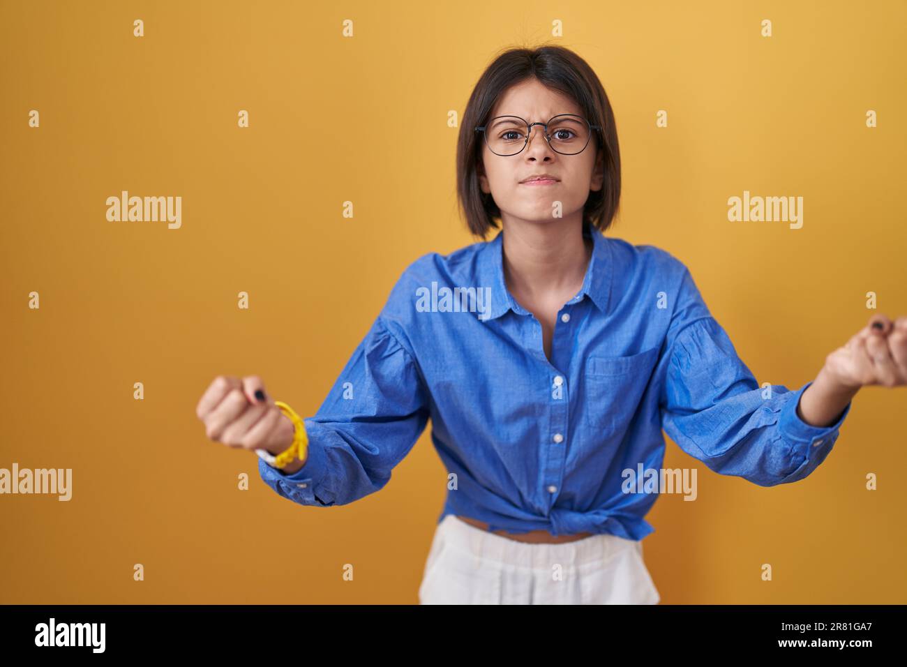 Young girl standing over yellow background angry and mad raising fists ...