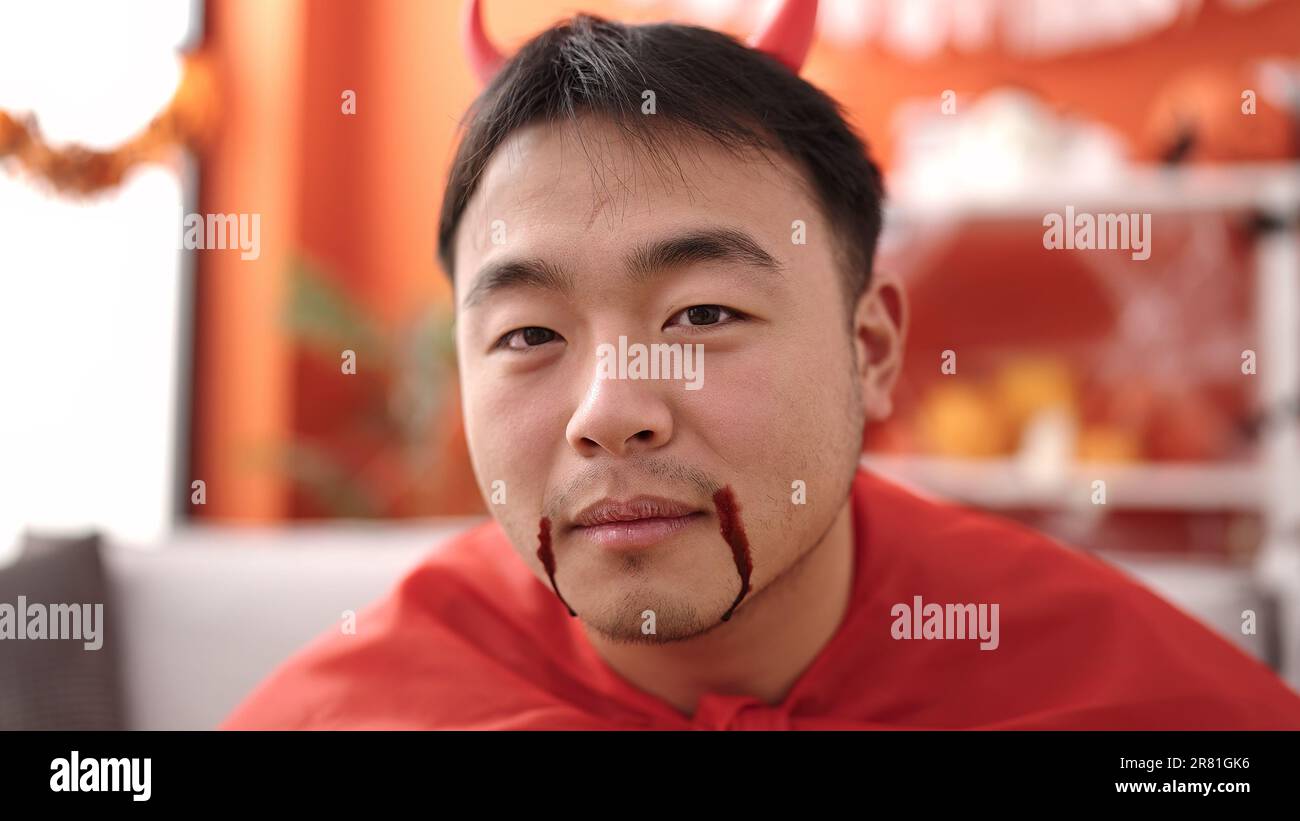 Young chinese man wearing devil costume having halloween party at home ...