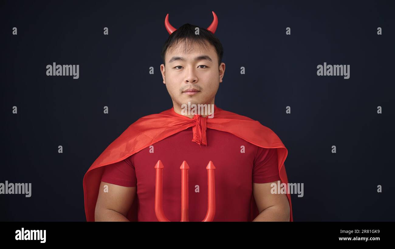 Young chinese man wearing devil costume holding trident over isolated ...