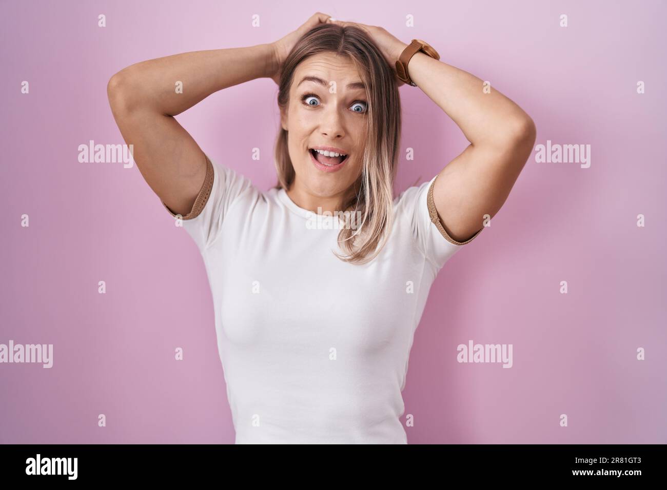 Blonde caucasian woman standing over pink background crazy and scared ...