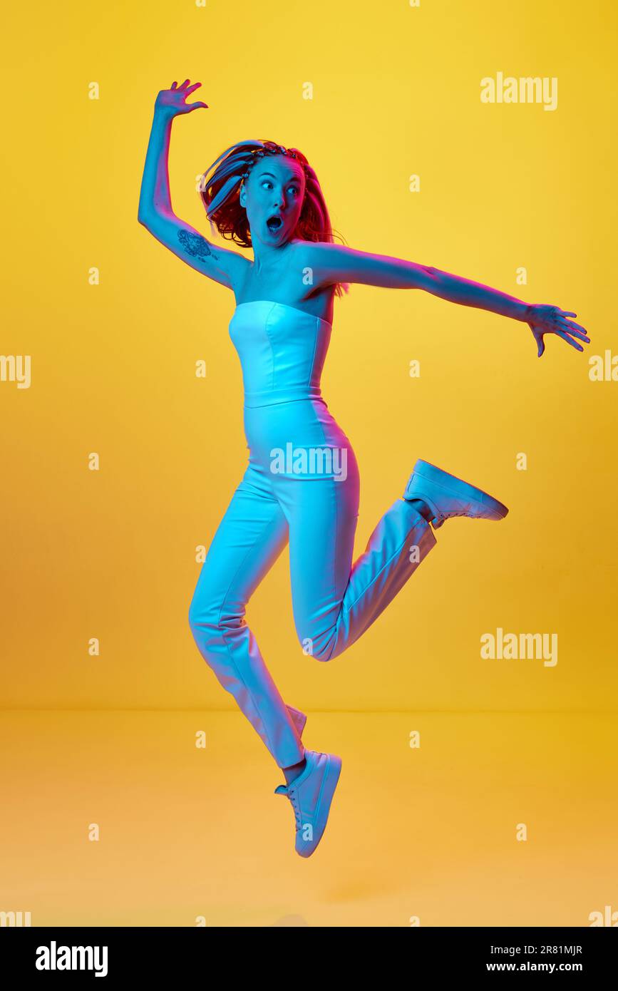 Full-length portrait of young emotional girl in white clothes jumping ...