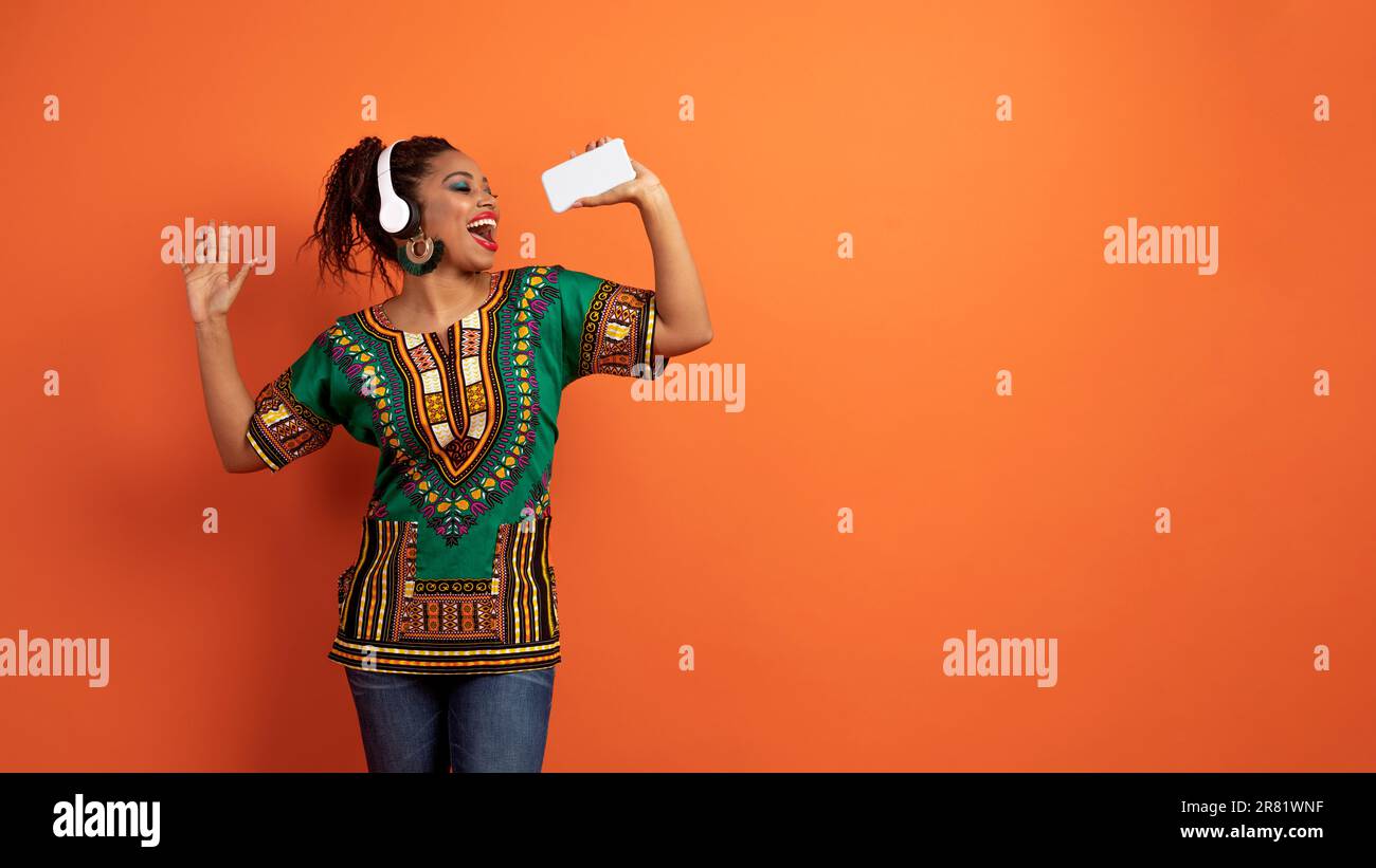 Happy black woman in african clothing singing, dancing on orange Stock ...