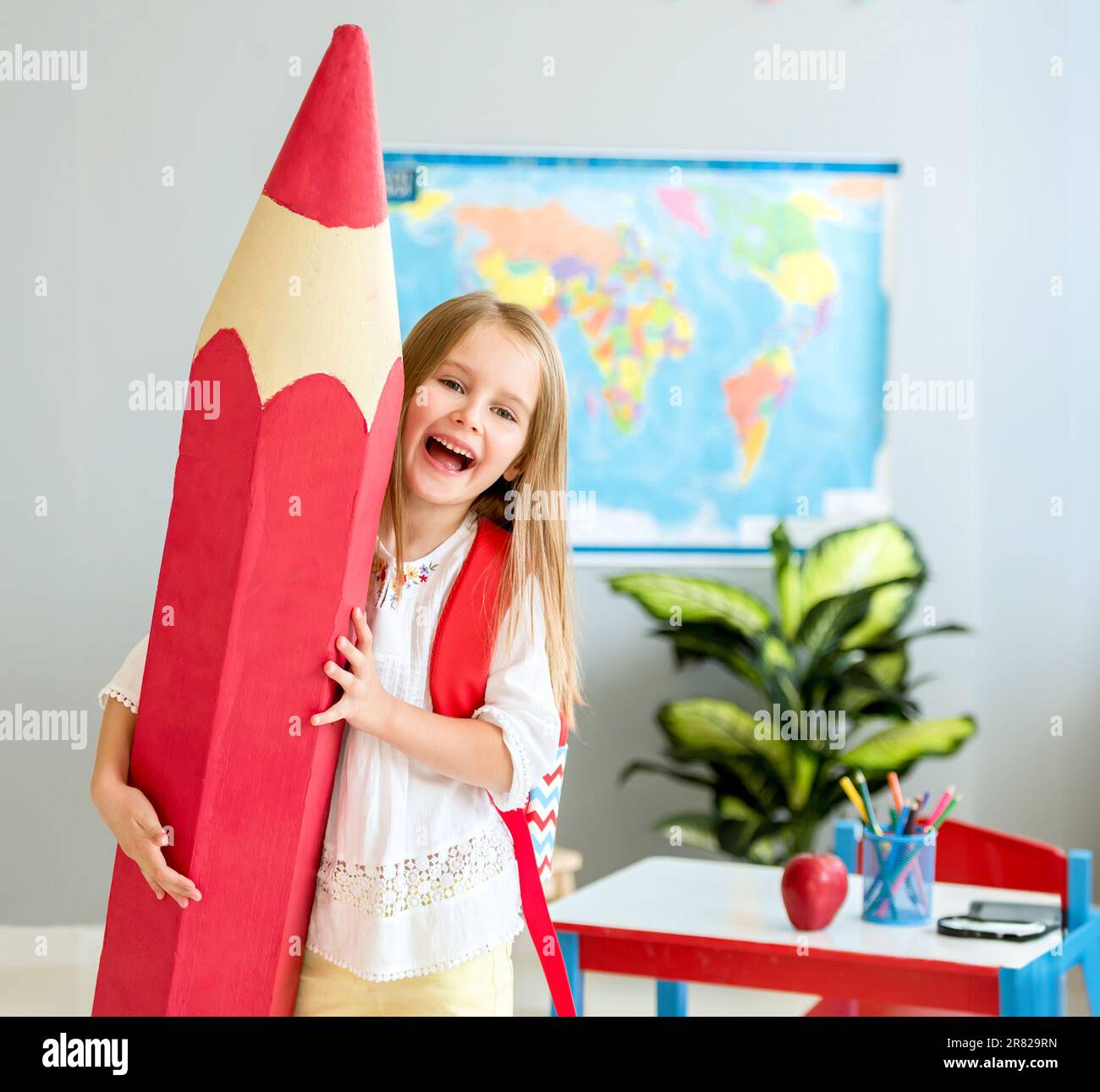 Little smiling blond girl with red bag holding huge red decorative ...