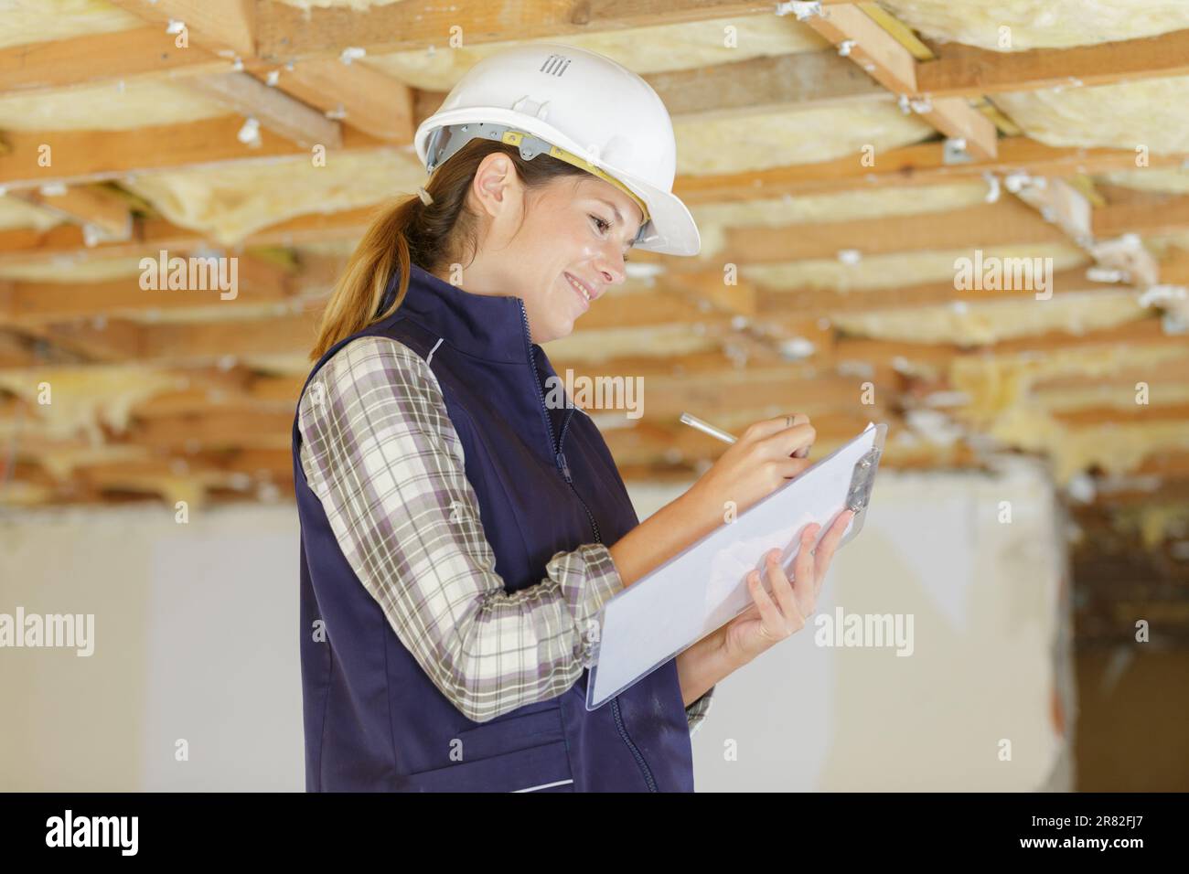 female builder making notes on clipboard at property under renovation ...