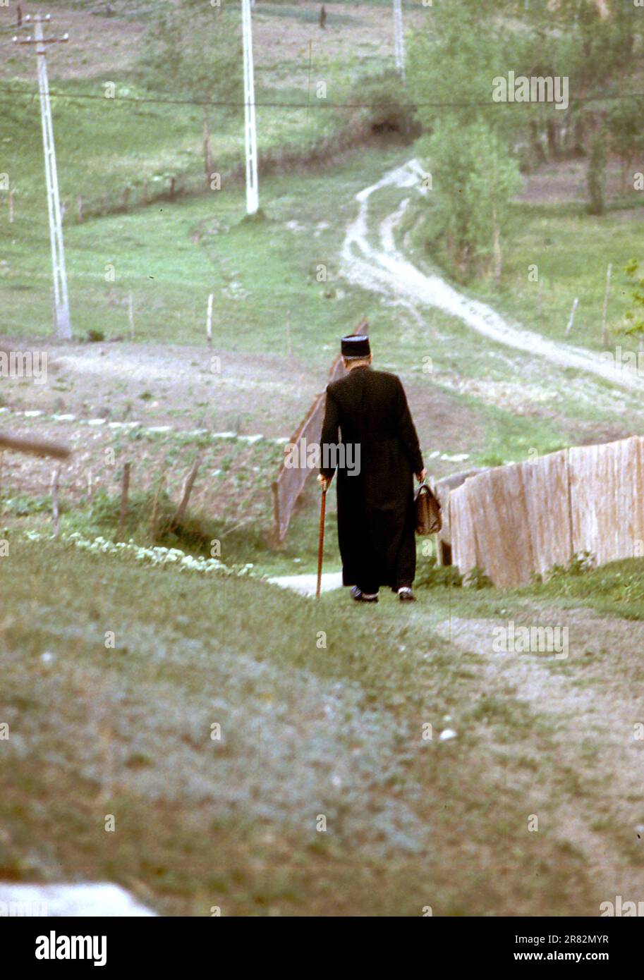 Elderly priest walking on a village lane in Romania's countryside ...