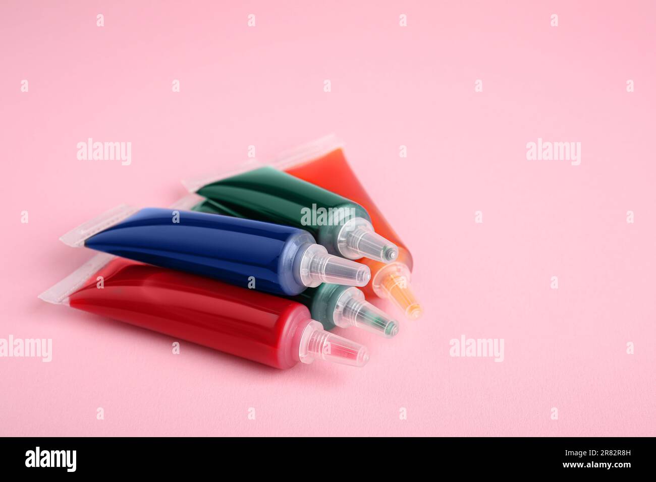 Tubes with different food coloring on pink background, space for text ...