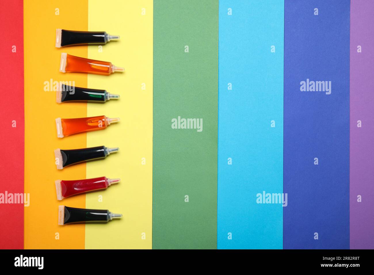 Tubes with different food coloring on rainbow background, flat lay ...