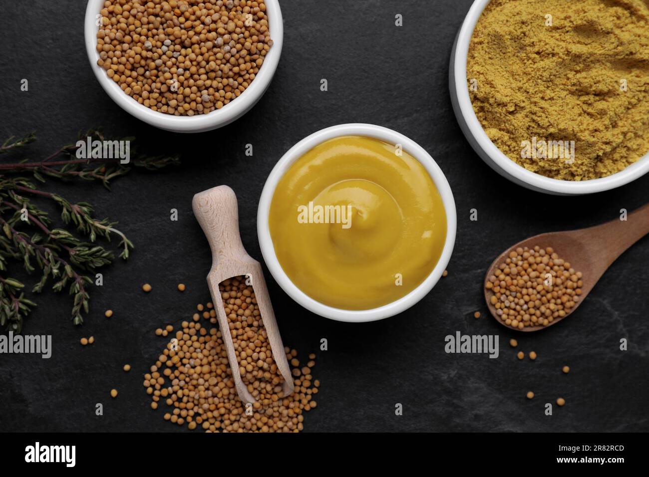 Delicious mustard, seeds and powder on black textured table, flat lay ...