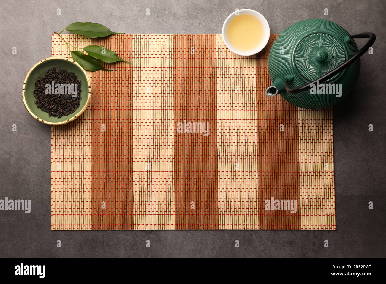Flat lay composition with bamboo mat, teapot and cup of tea on grey ...