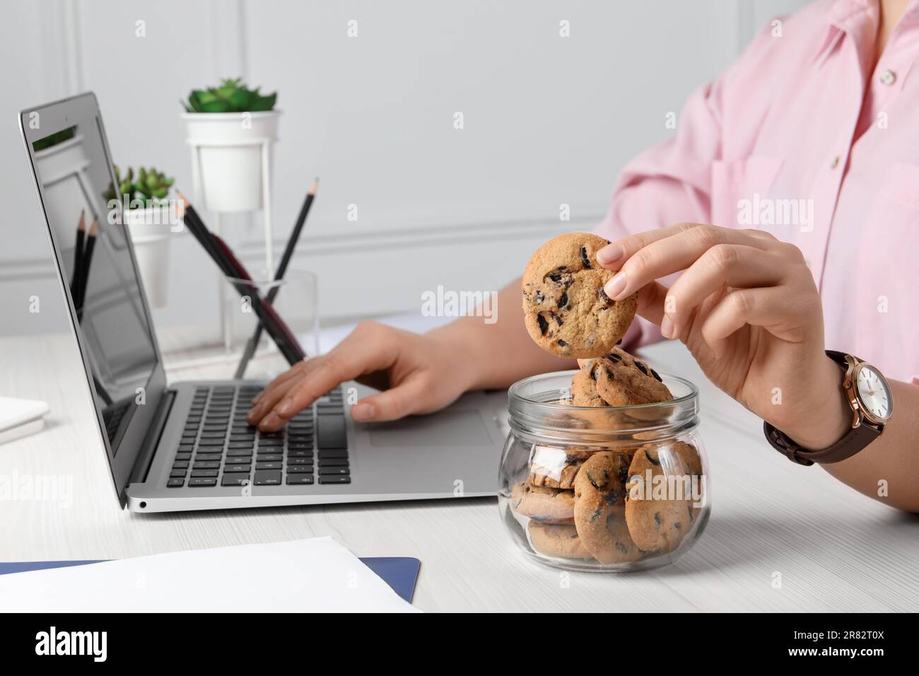 Office worker taking chocolate chip cookie from jar at workplace ...